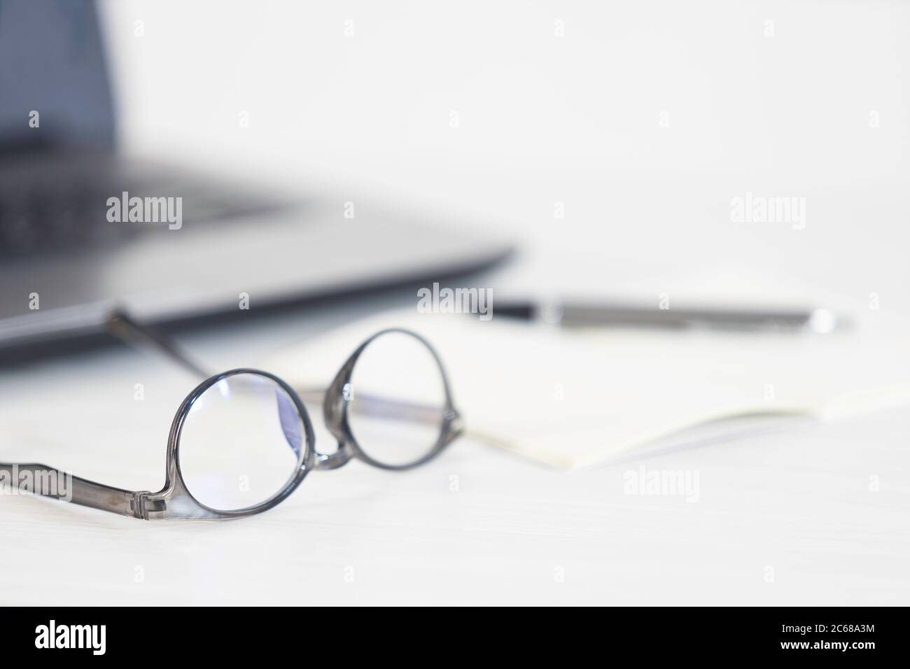 Eyeglasses, open notebook, pen and laptop on the office table. Top view ...