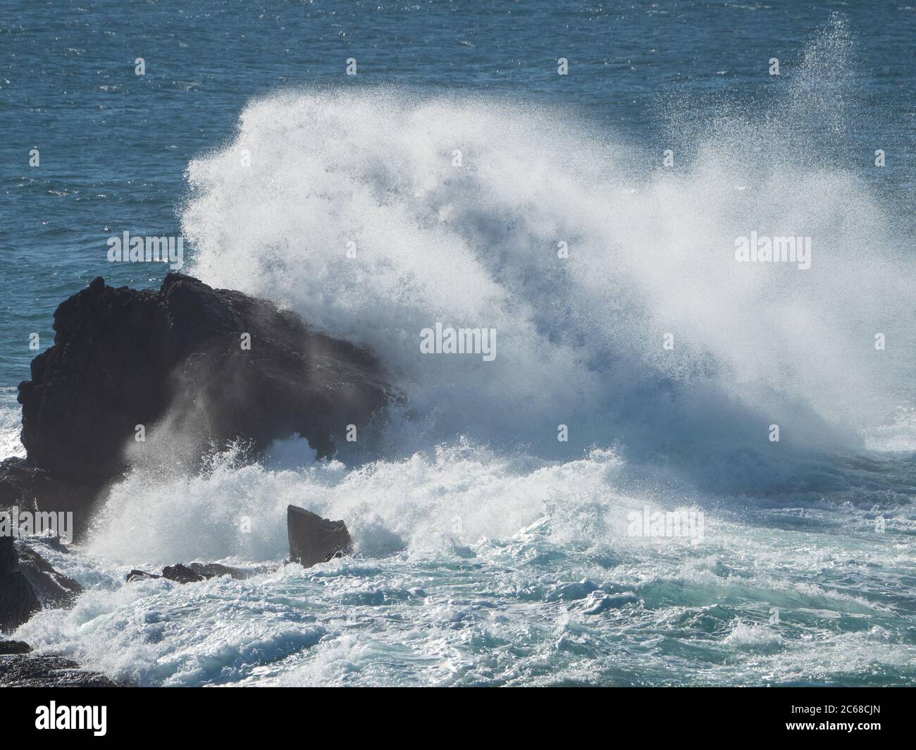 Wave reaching up into the air as its crashing and explodes over rocks ...
