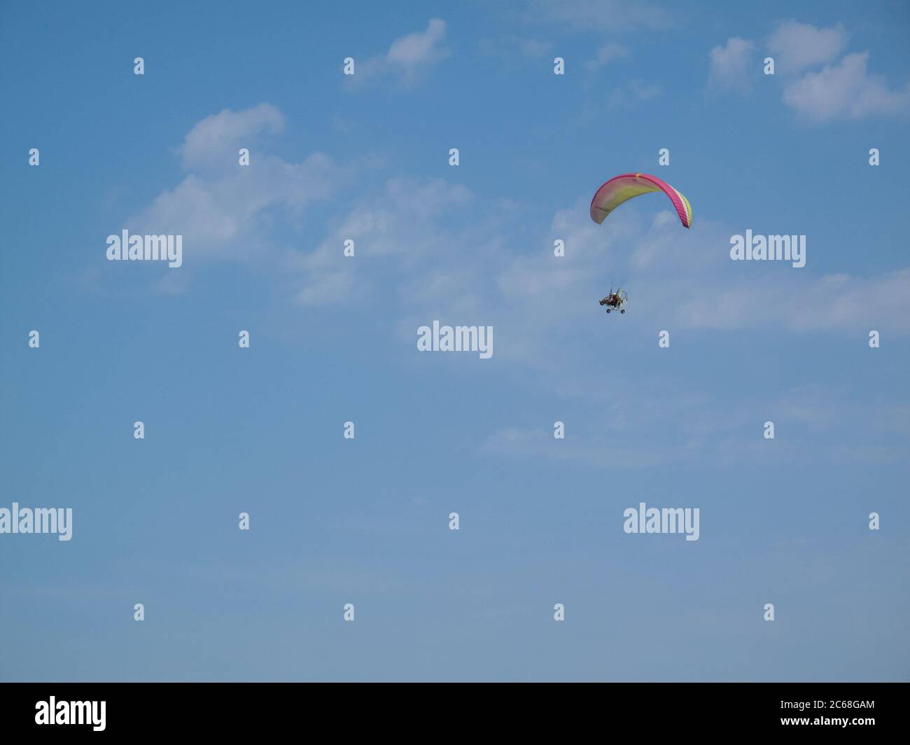 A paraglider flies in the sky under a multi-colored paraglider ...