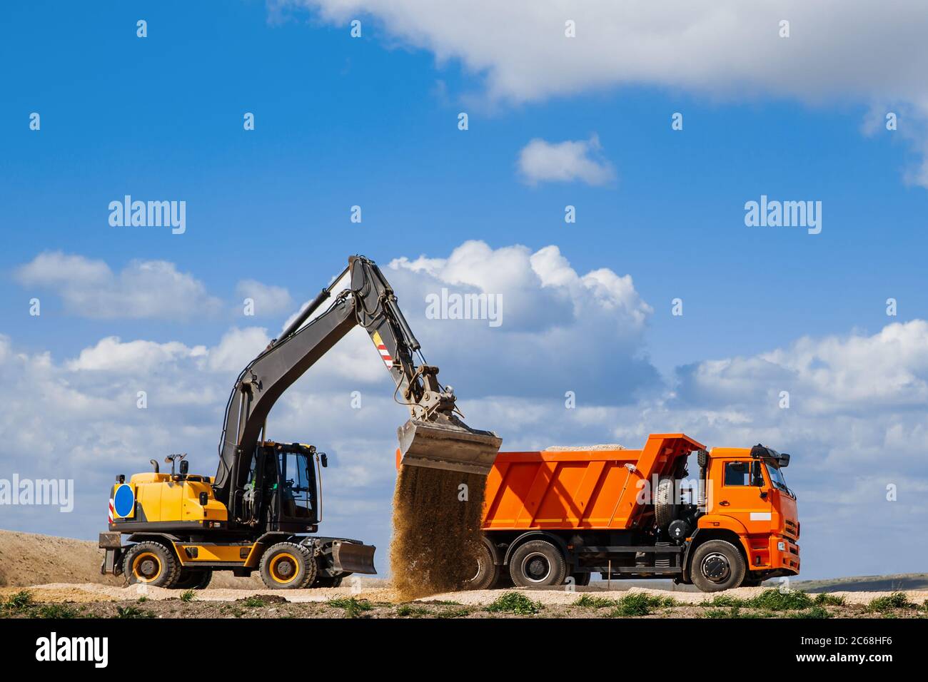 A yellow backhoe loader loads the earth into a truck during the ...