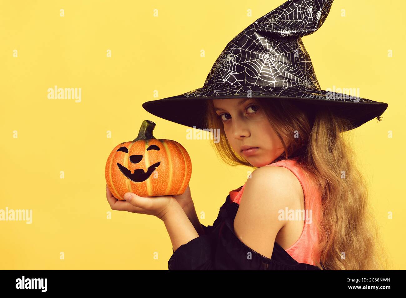 Child in witch costume and jack o lantern. Girl with carved orange pumpkin isolated on warm ...