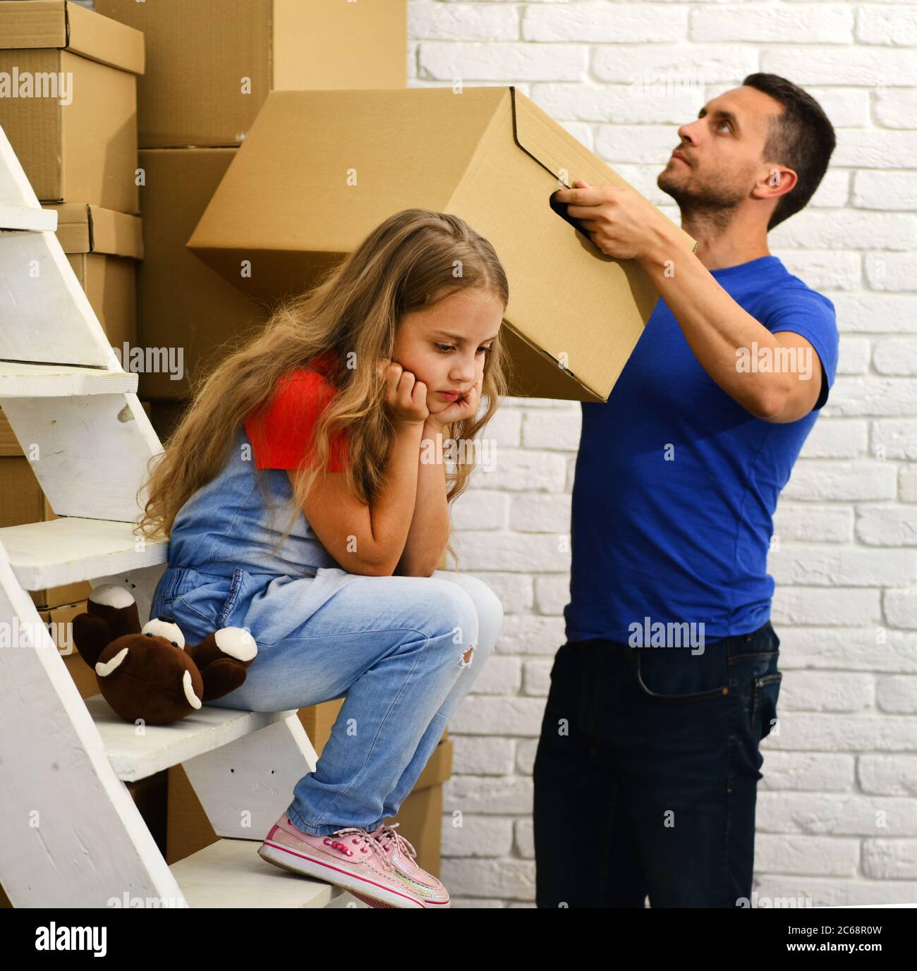 Deliveryman and child with sad face. Man puts box up into stack on ...