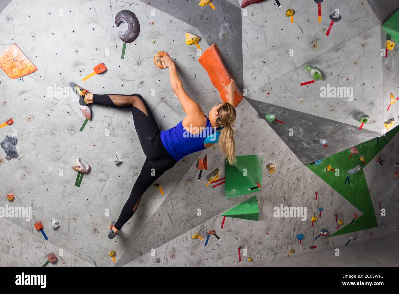 Rock climber woman hanging on a bouldering climbing wall, inside on ...