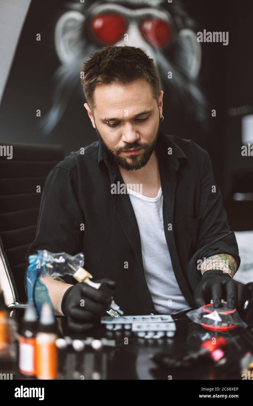 Professional tattooer in black gloves holding tattoo machine in hand ...