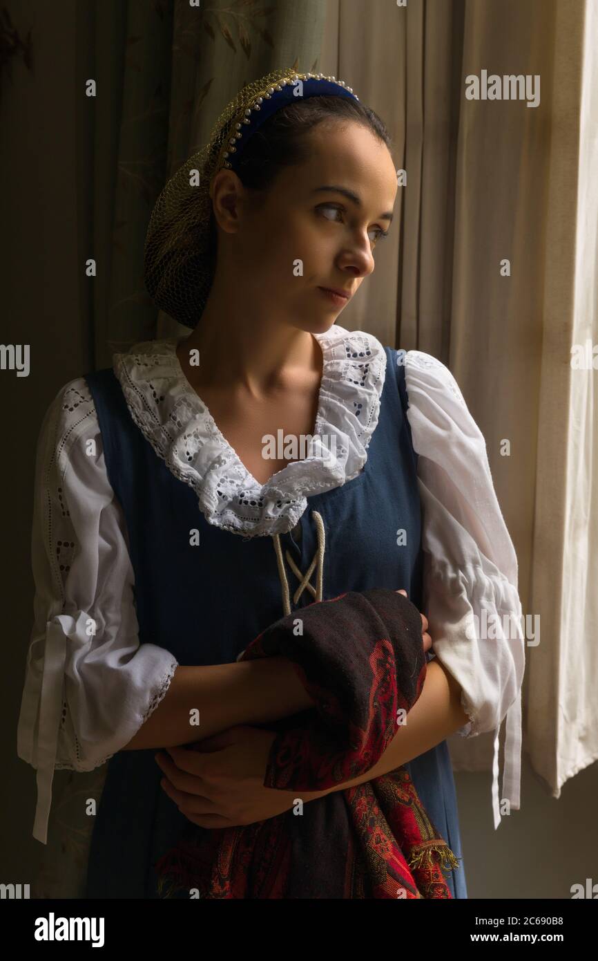 Pretty young woman in Renaissance costume looking through window of a ...