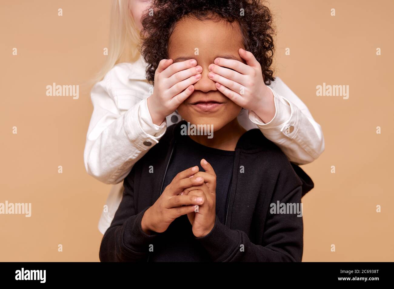 unrecognizable kid girl with pale skin closing afro boy's eyes from ...