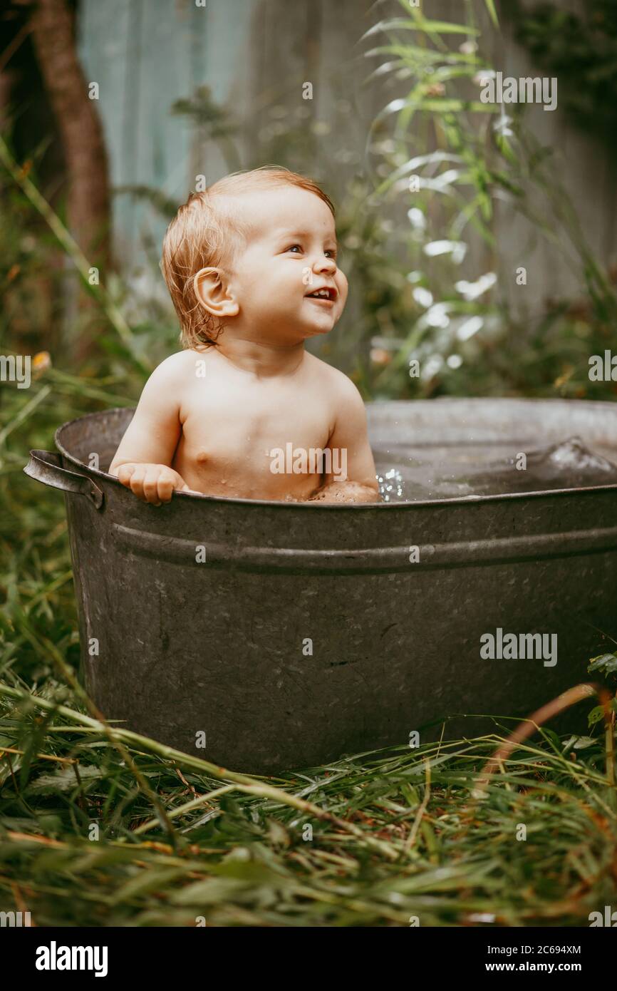 Cute funny little boy bathing in galvanized tub outdoor in green garden ...