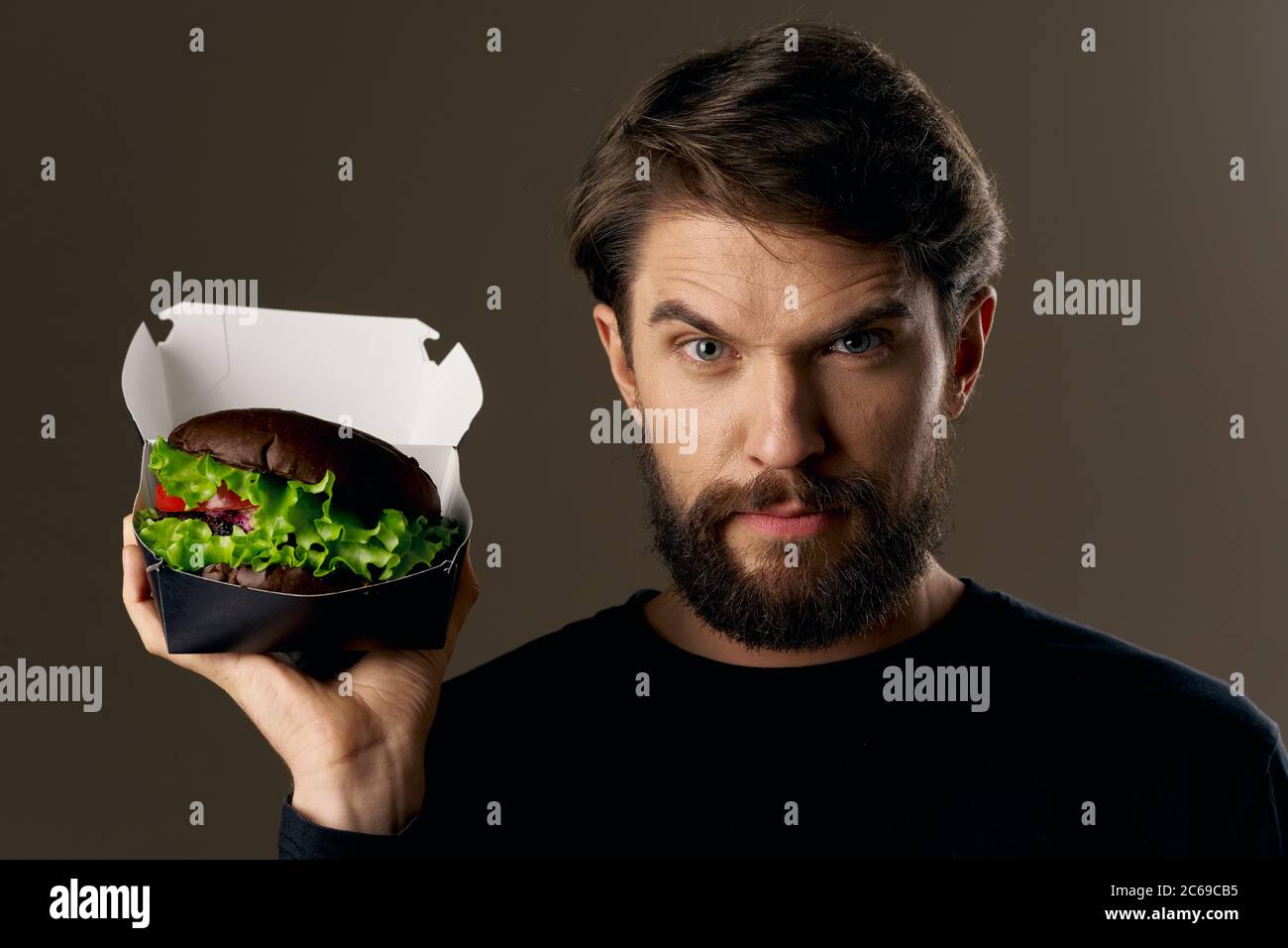 Handsome guy with a hamburger in his hand against a dark background ...