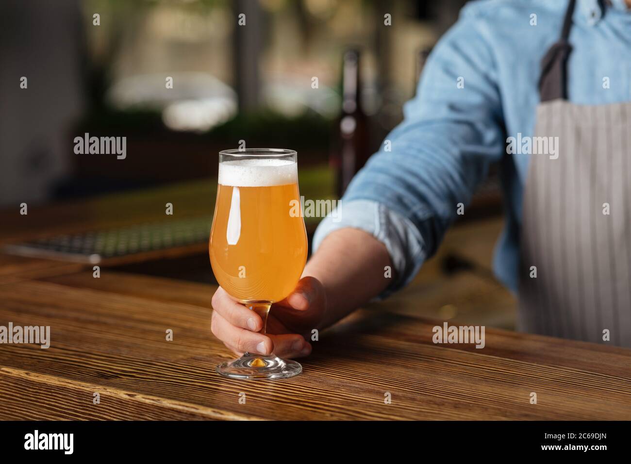 Art of brewing. Barman in apron put on wooden table glass of light ...