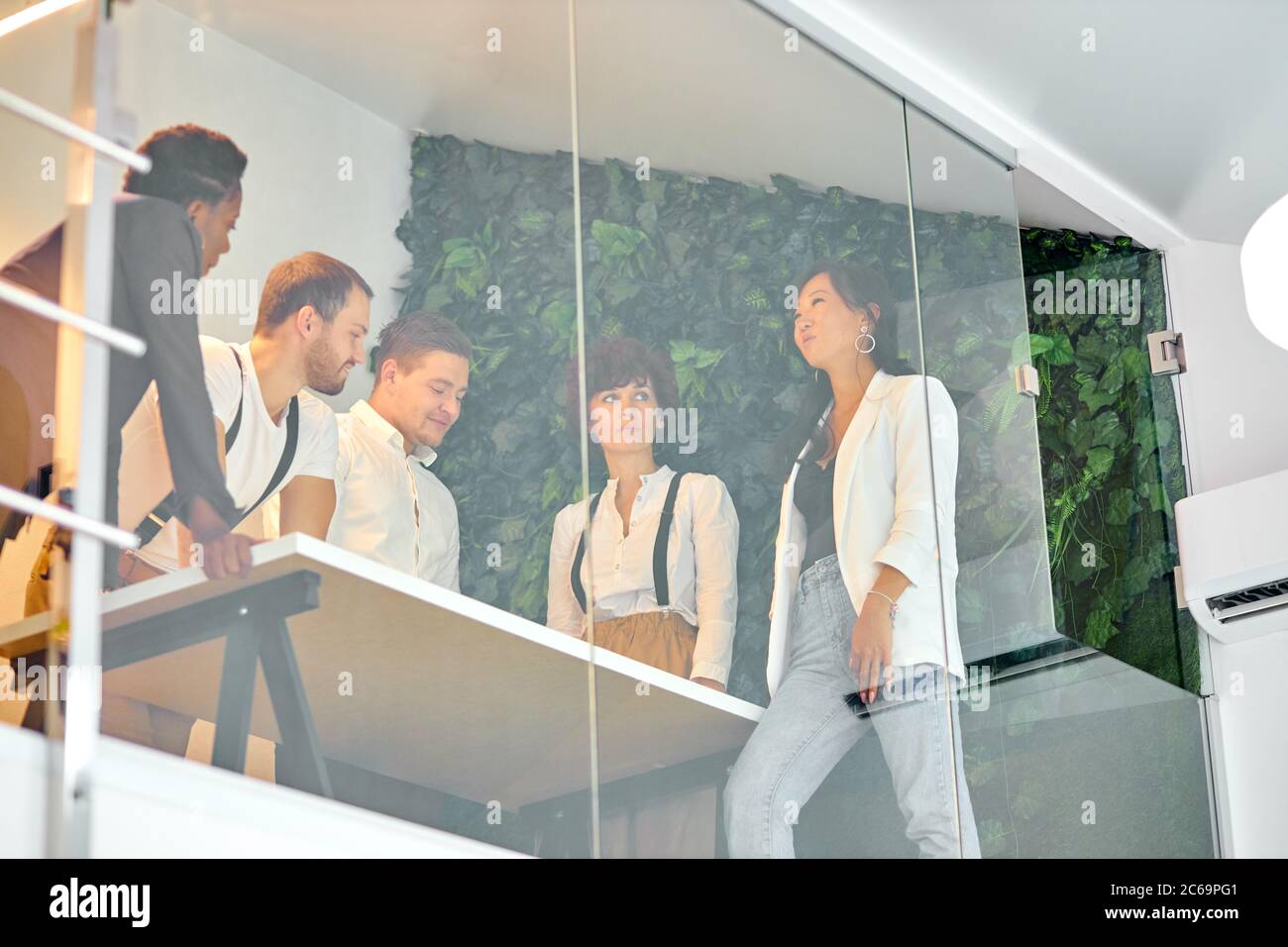 Diverse co-workers, partners stand round table talking with each other ...