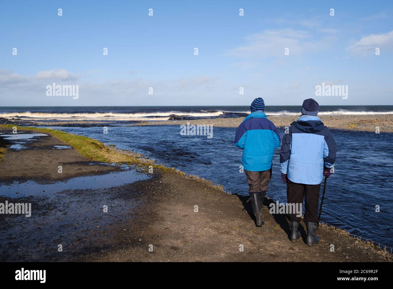 Two friends walk alongside the banks of the River Bush looking out to ...