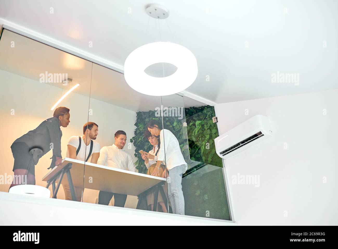 Diverse co-workers, partners stand round table talking with each other ...