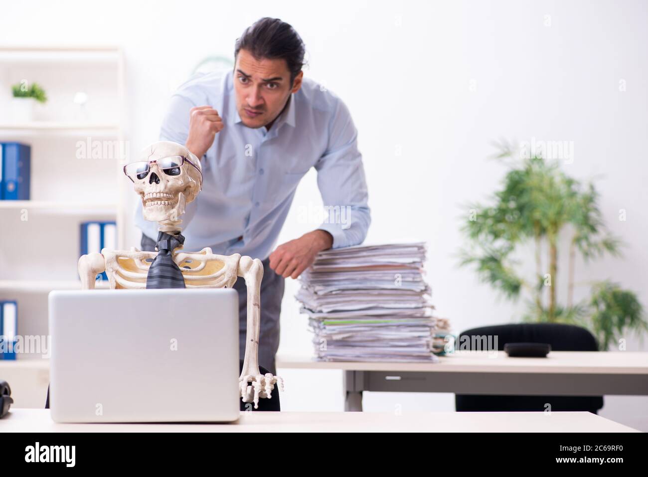 Young employee and skeleton in the office Stock Photo - Alamy