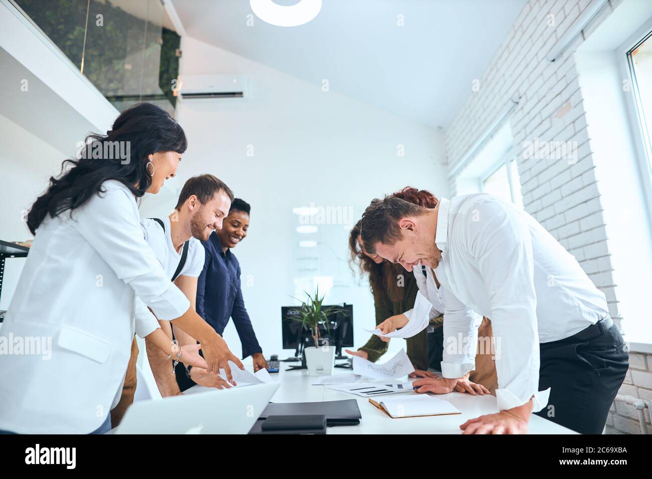 Multiethnic group of people stand around table enjoying meeting, smile ...