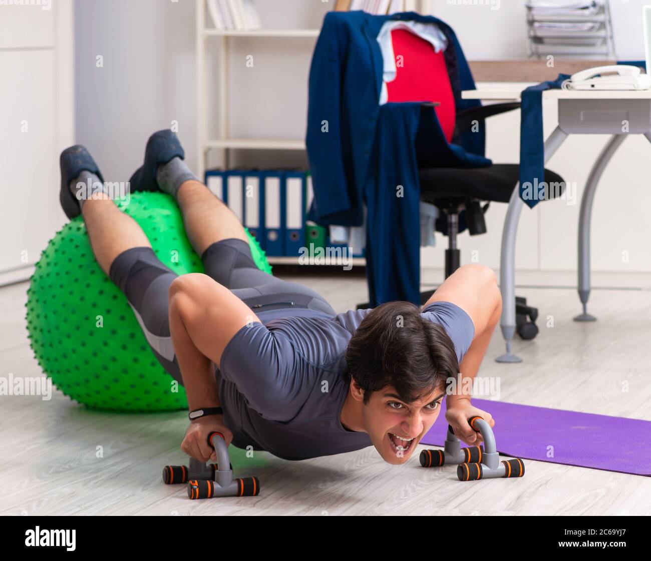 The young male employee exercising in the office Stock Photo - Alamy