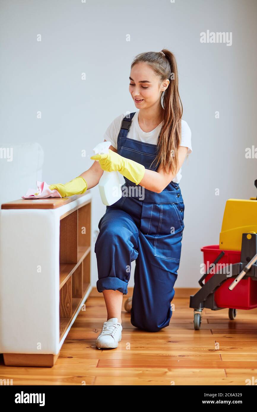 Young caucasian female janitor in yellow rubber gloves use spray and ...