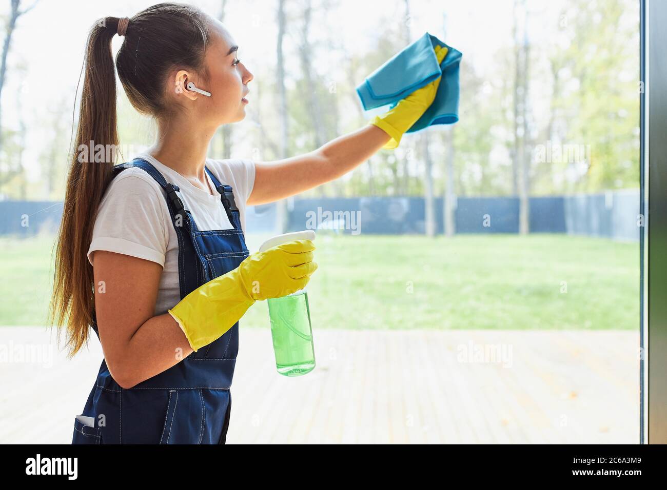 Caucasian cleaner in uniform wearing headphones stand washing panoramic ...