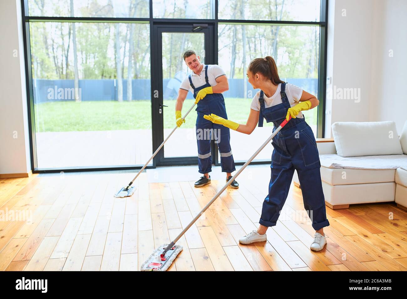 Effective job mopping wooden floor in apartment, two caucasians in blue ...