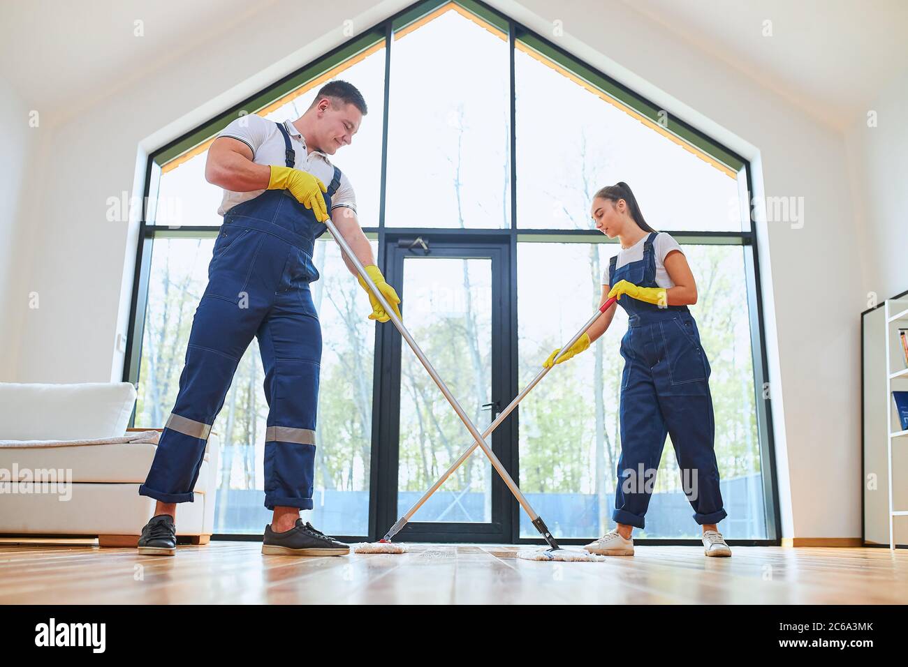 Effective job mopping wooden floor in apartment, two caucasians in blue ...