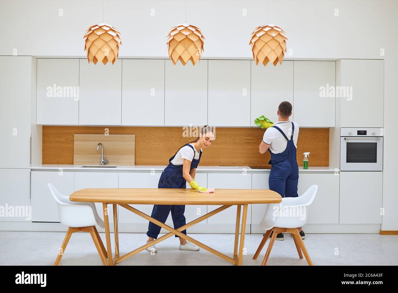 Caucasian cleaners in blue uniform wiping dust off kitchen table and ...