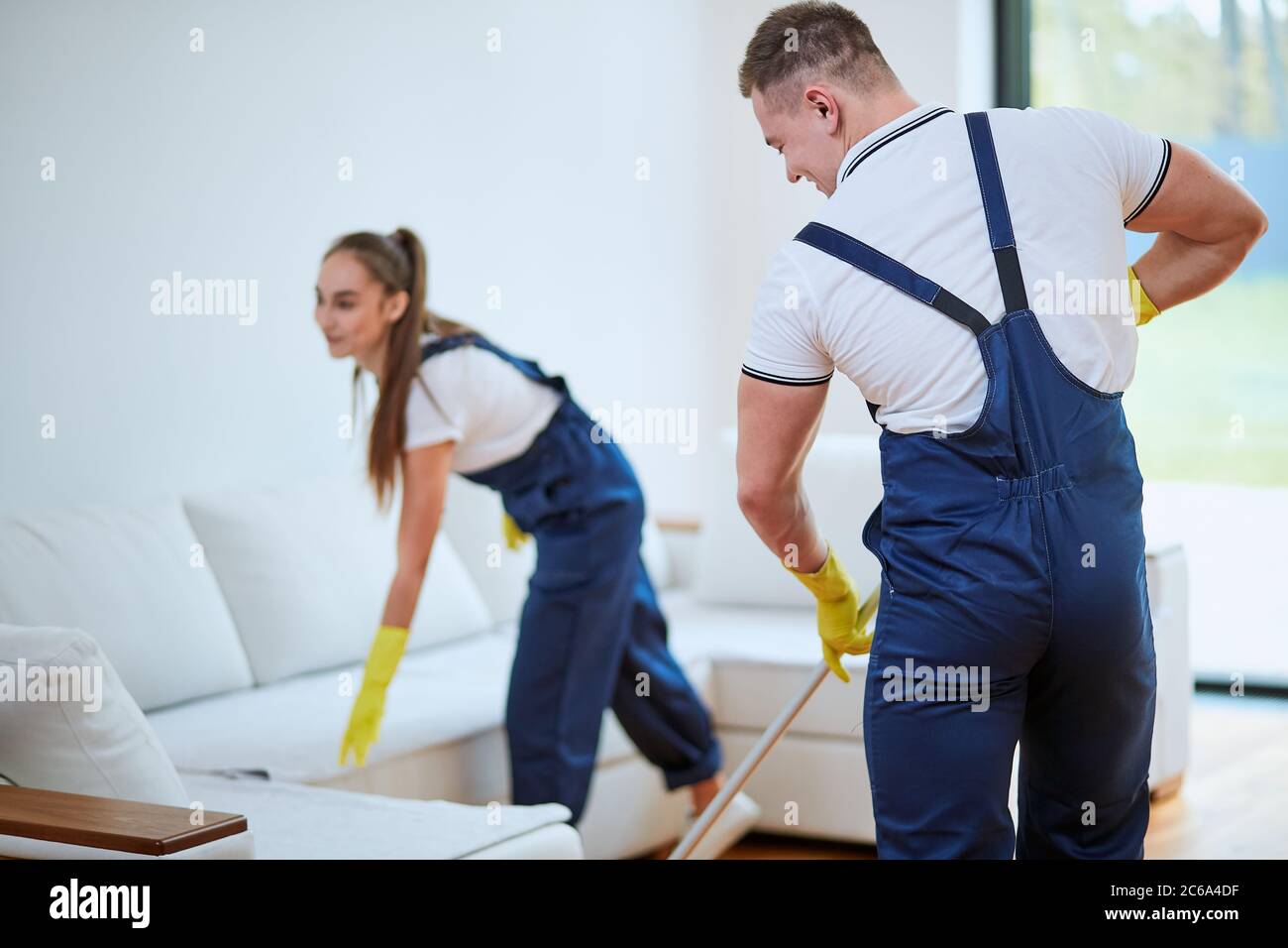 Two janitors washing floor near sofa. man and woman in uniform ...