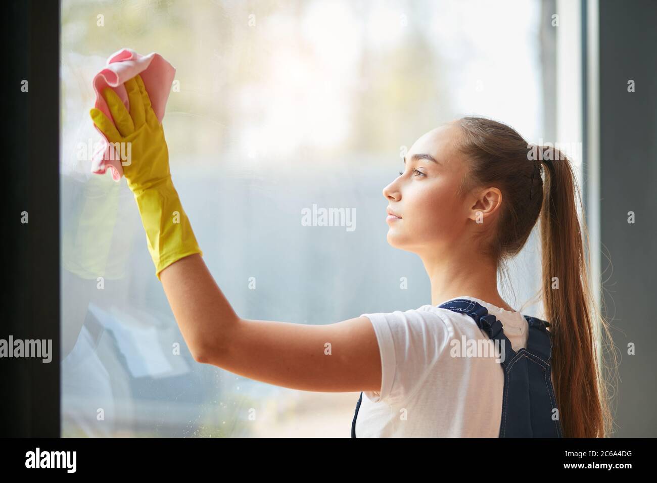 Young long haired girl cleaning panoramic window with yellow gloves ...