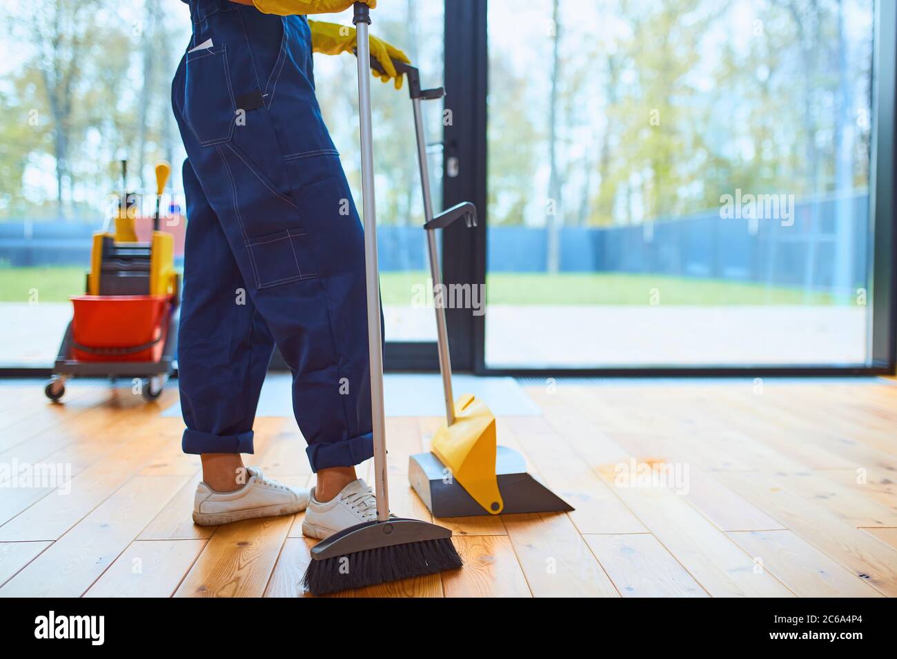 Side view on young cleaner sweeping the floor in living room, panoramic ...