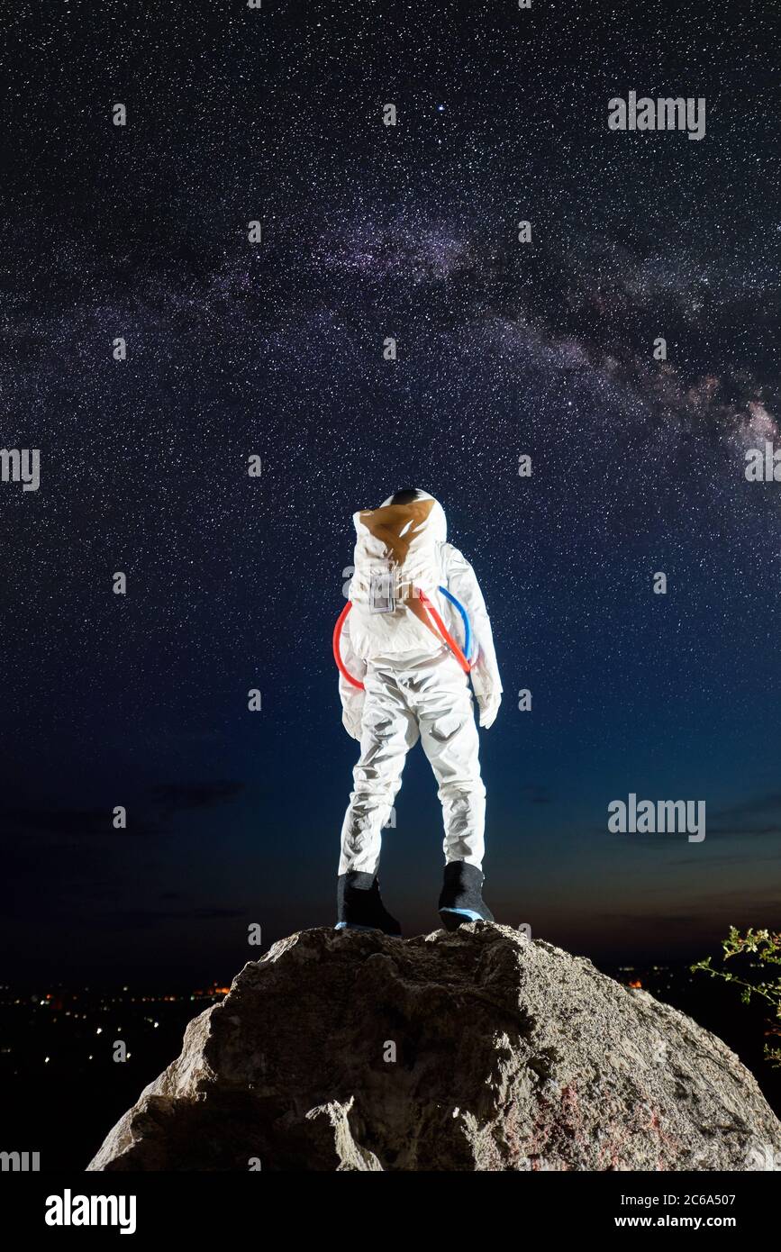 Back view of spaceman standing on top of rocky mountain and looking at ...