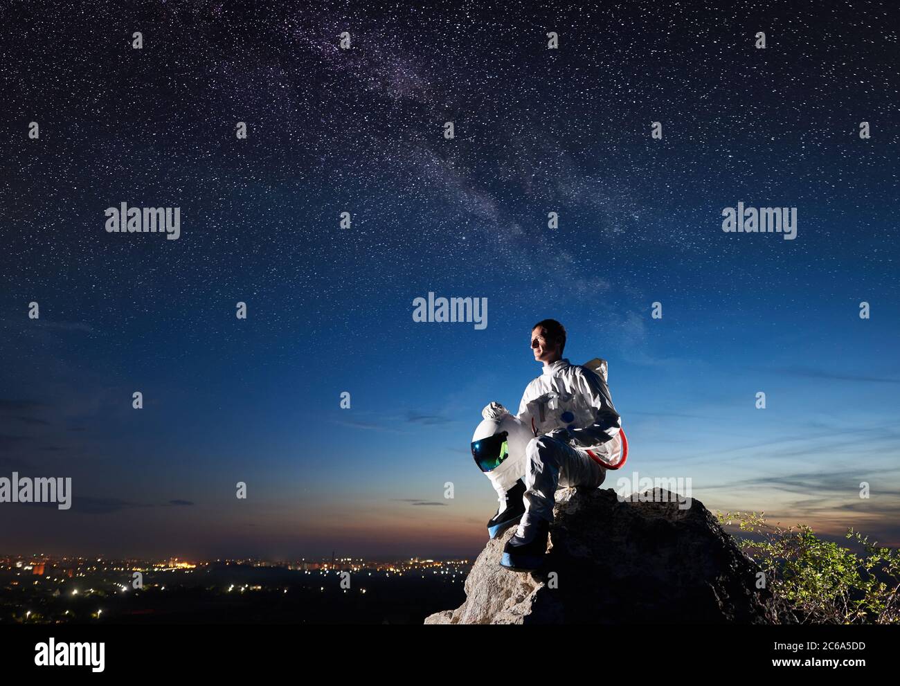 Side view of astronaut sitting on top of rocky hill and looking at ...
