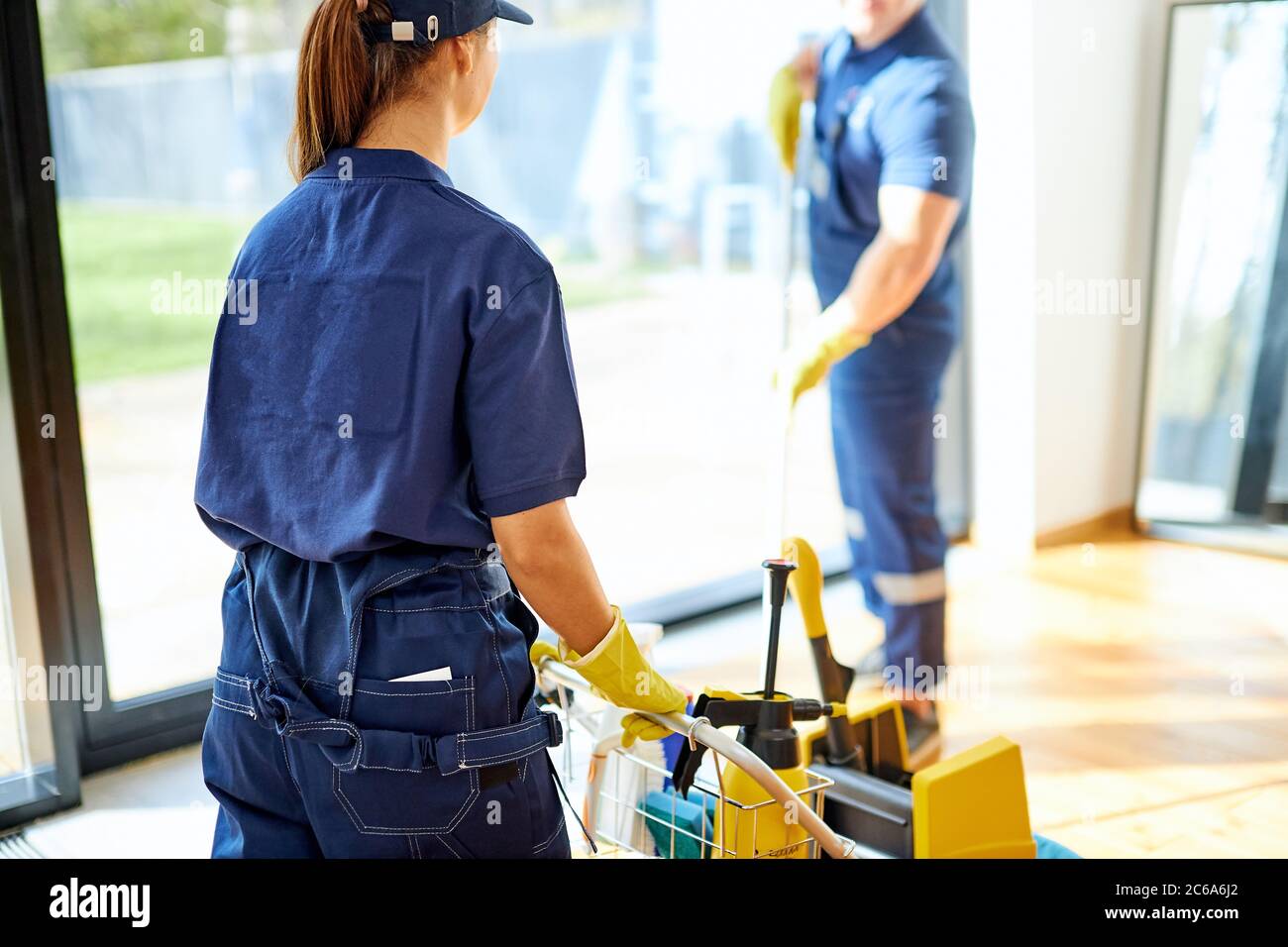 Back view on two janitors in blue working uniform clean up roon with ...