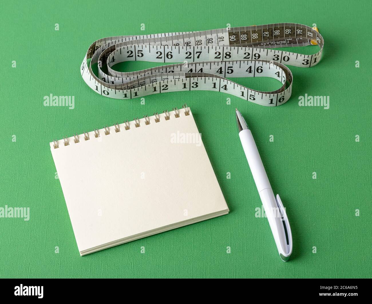 Measuring tape with centimeters and inches, paper notepad and white pen ...