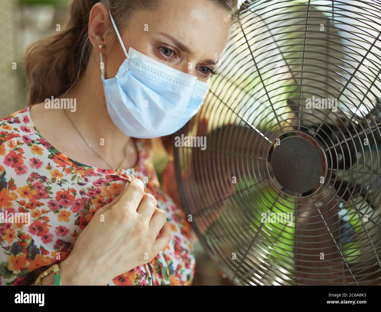 Summer heat. sad middle aged woman in floral blouse with electric fan ...