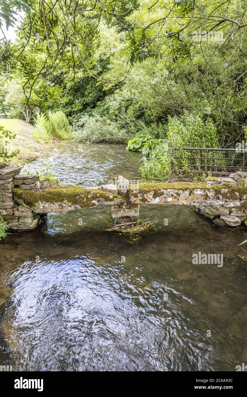 A tiny stone clapper bridge over the infant River Windrush as it flows ...