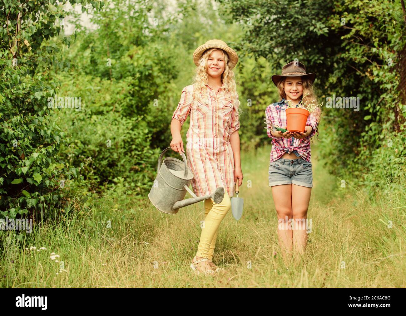 Girls in hats planting plants. Sisters helping at farm. Family farm ...