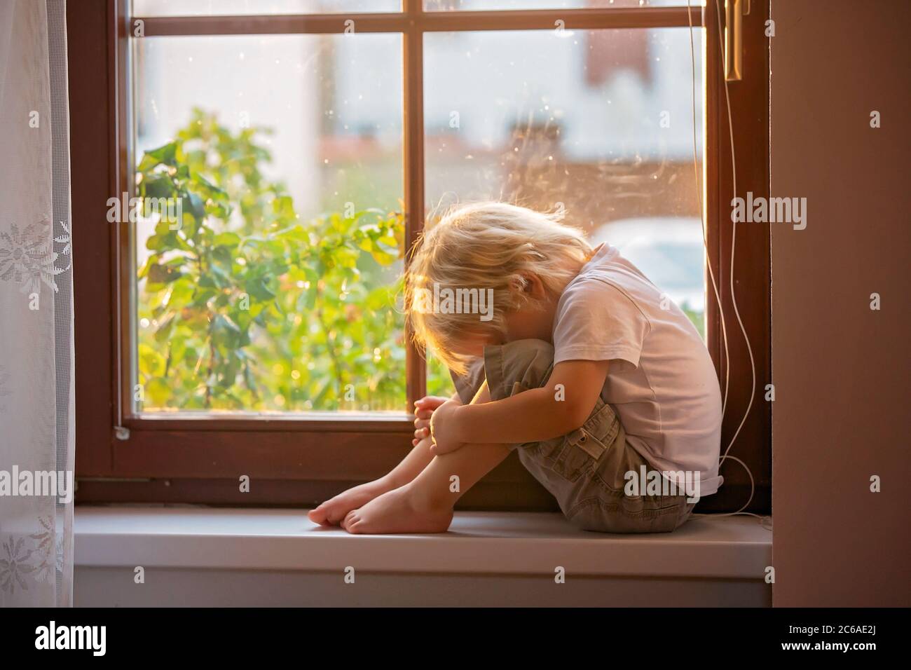 Abandoned little toddler boy, sitting sad on a window shield, looking ...