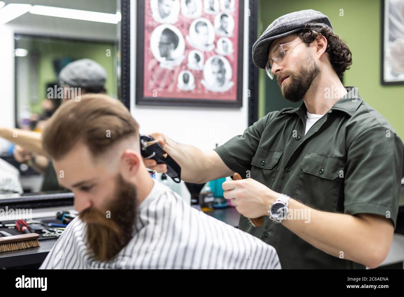 The hands of young barber making haircut to attractive man in ...