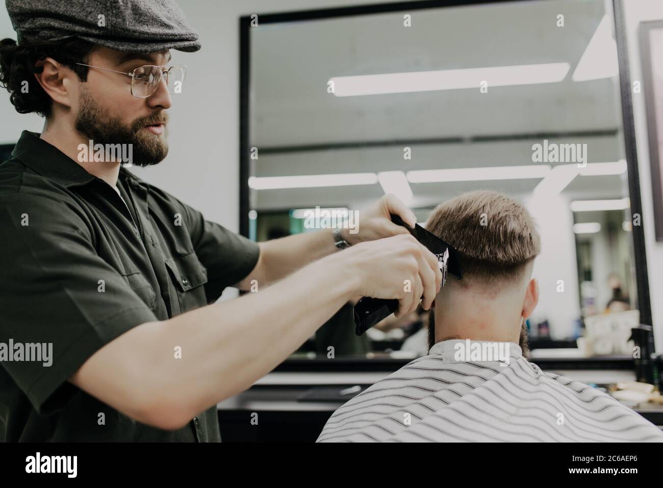 Young bearded man getting haircut by hairdresser while sitting in chair ...