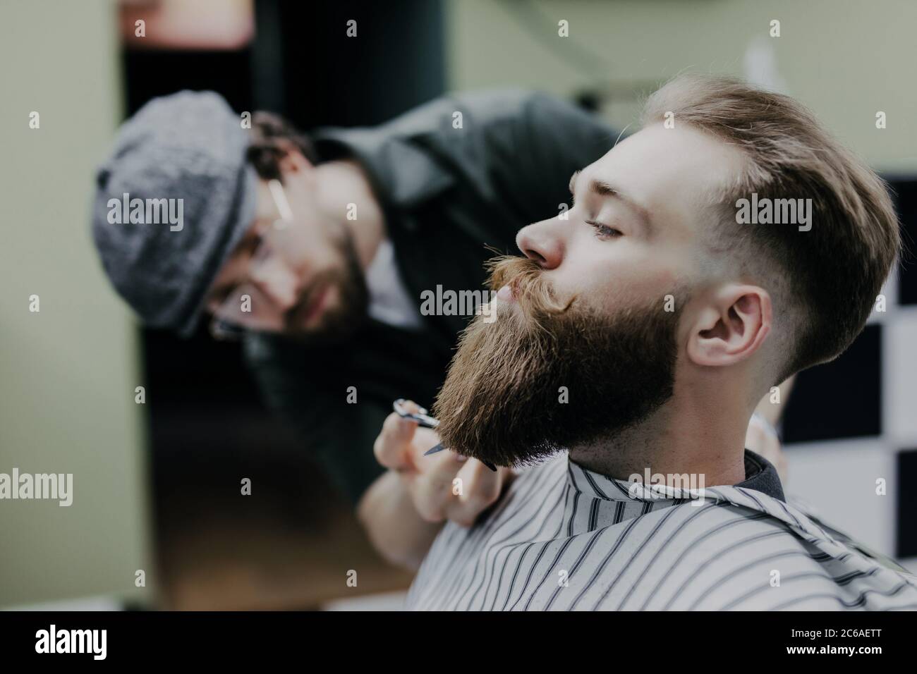 Side view of bearded man having his beard cut by hairdresser at the ...