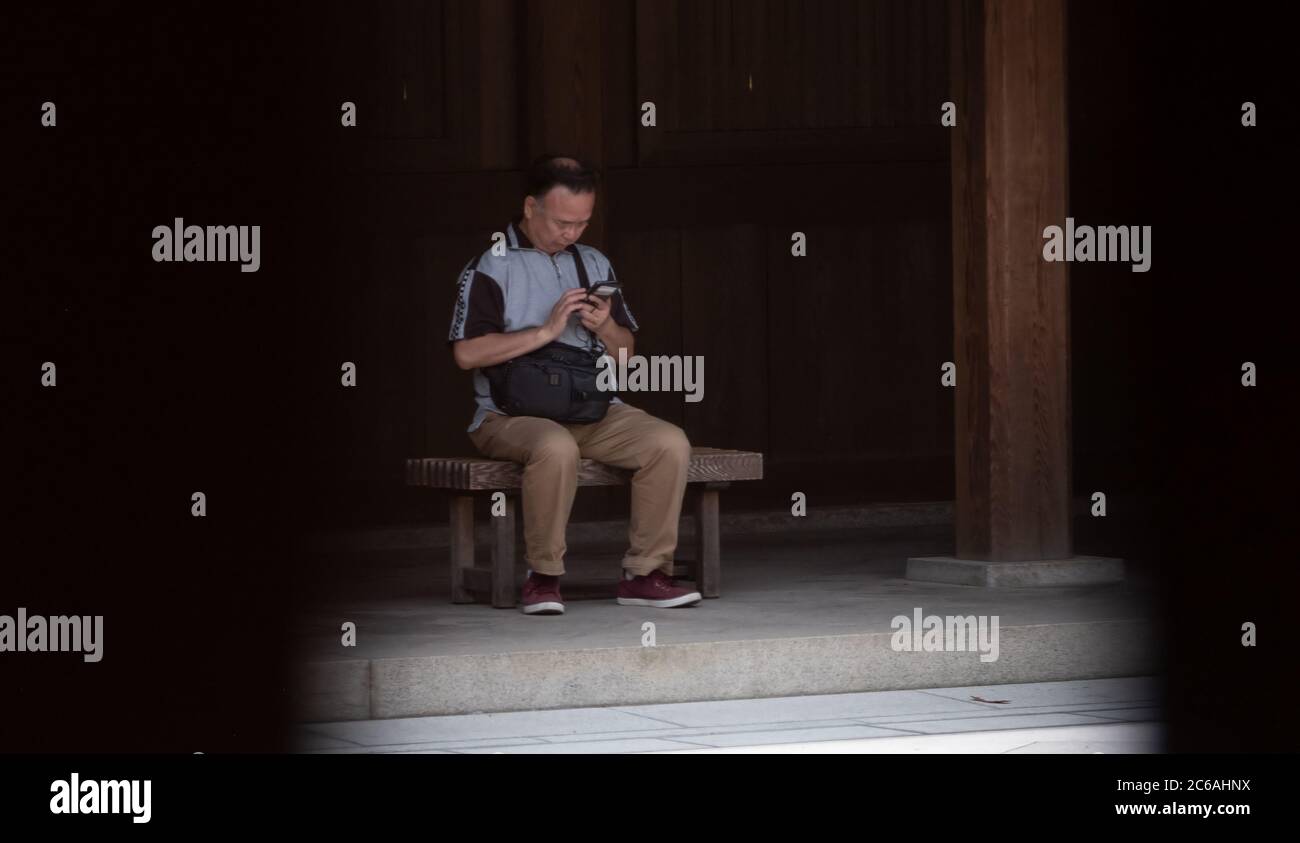 Elderly Japanese man sitting on a wooden bench with smartphone in Meiji ...