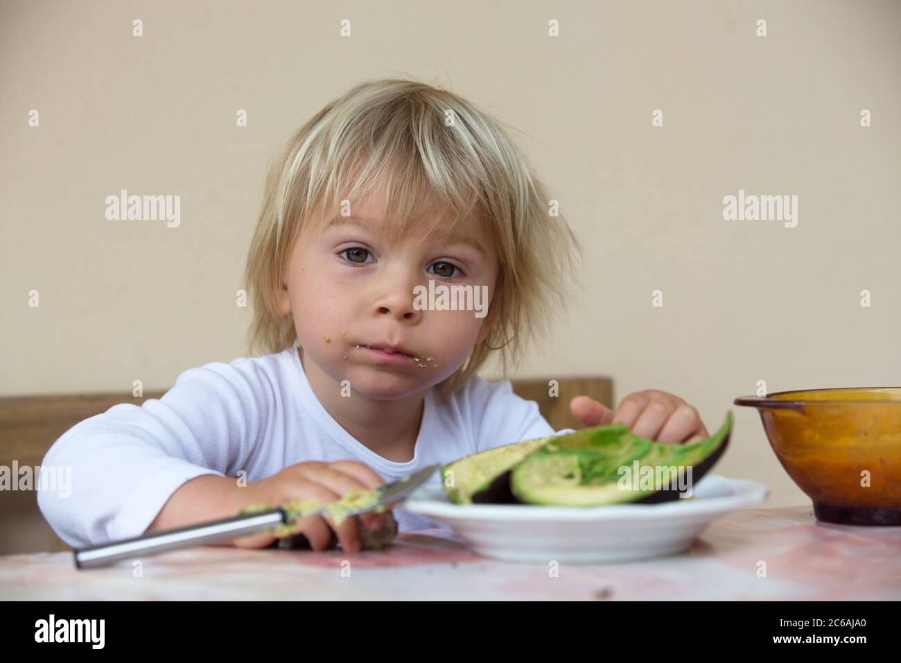 Cute blond child, boy eating avocado with spoon, healthy eating Stock ...