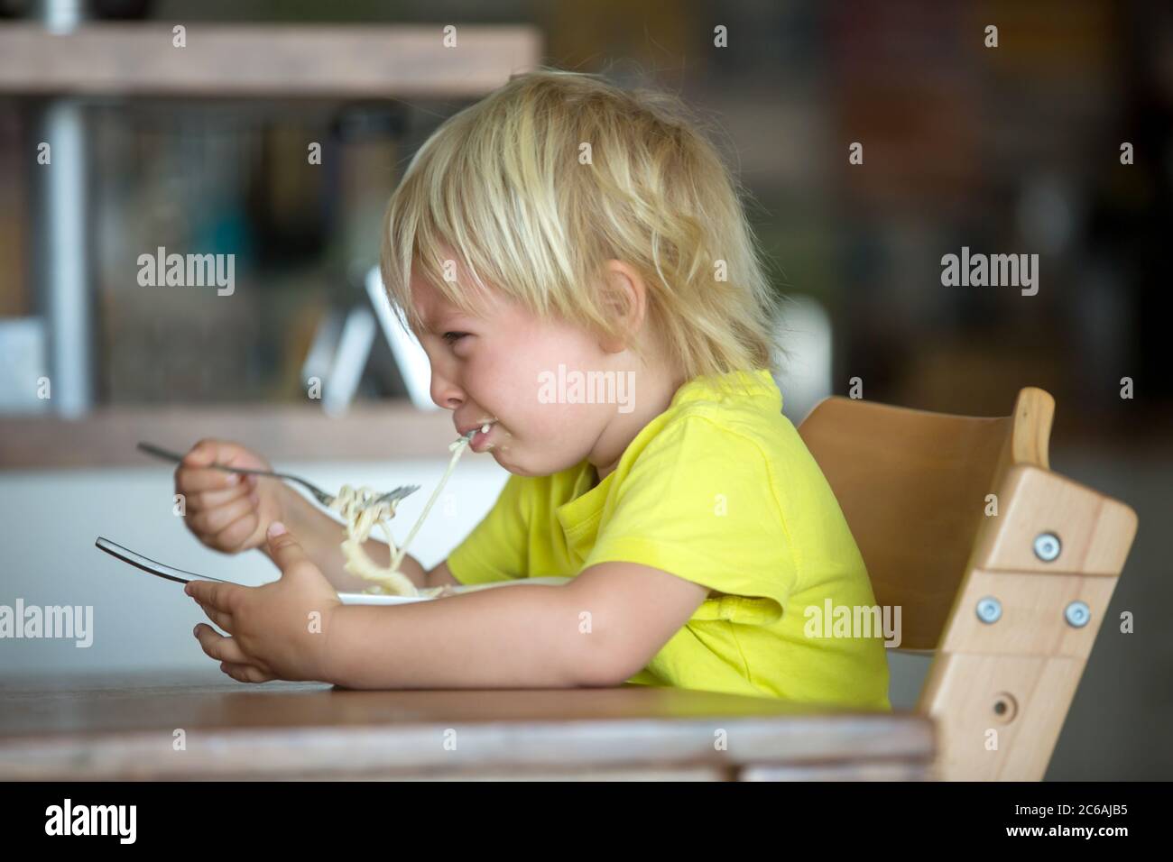 Cute blond boy, child eating spaghetti, crying with tantrum at home ...