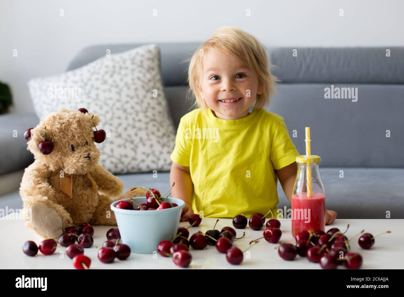 Toddler blond child, cute boy, eating cherries with teddy bears at home ...