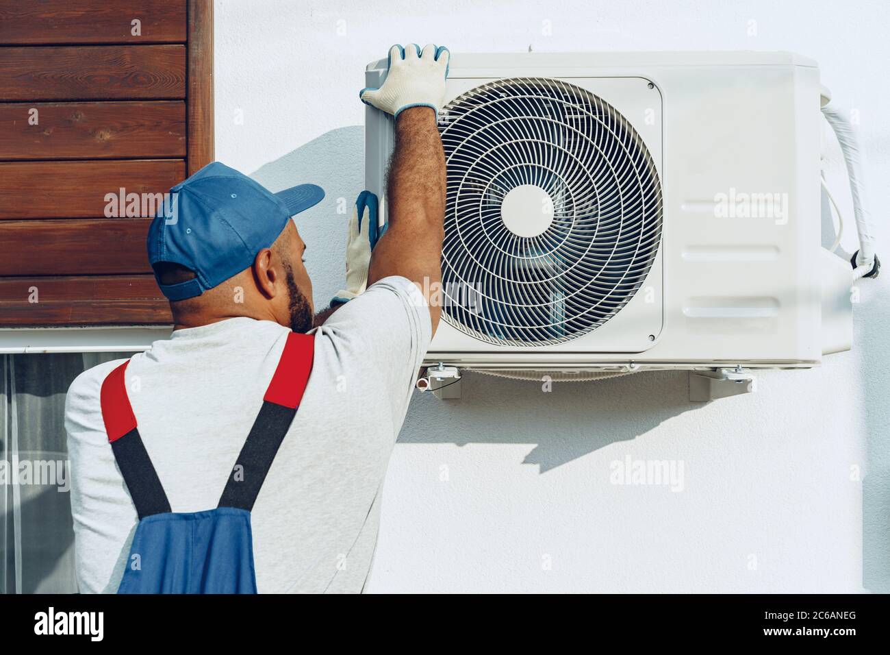 Repairman in uniform installing the outside unit of air conditioner ...