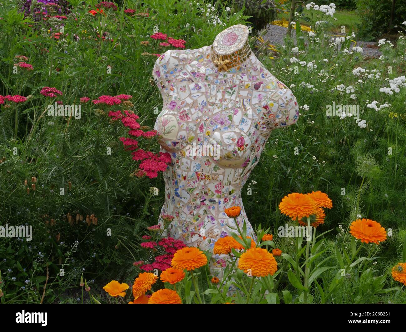 Mosaic garden sculpture of female torso surrounded by garden flowers ...