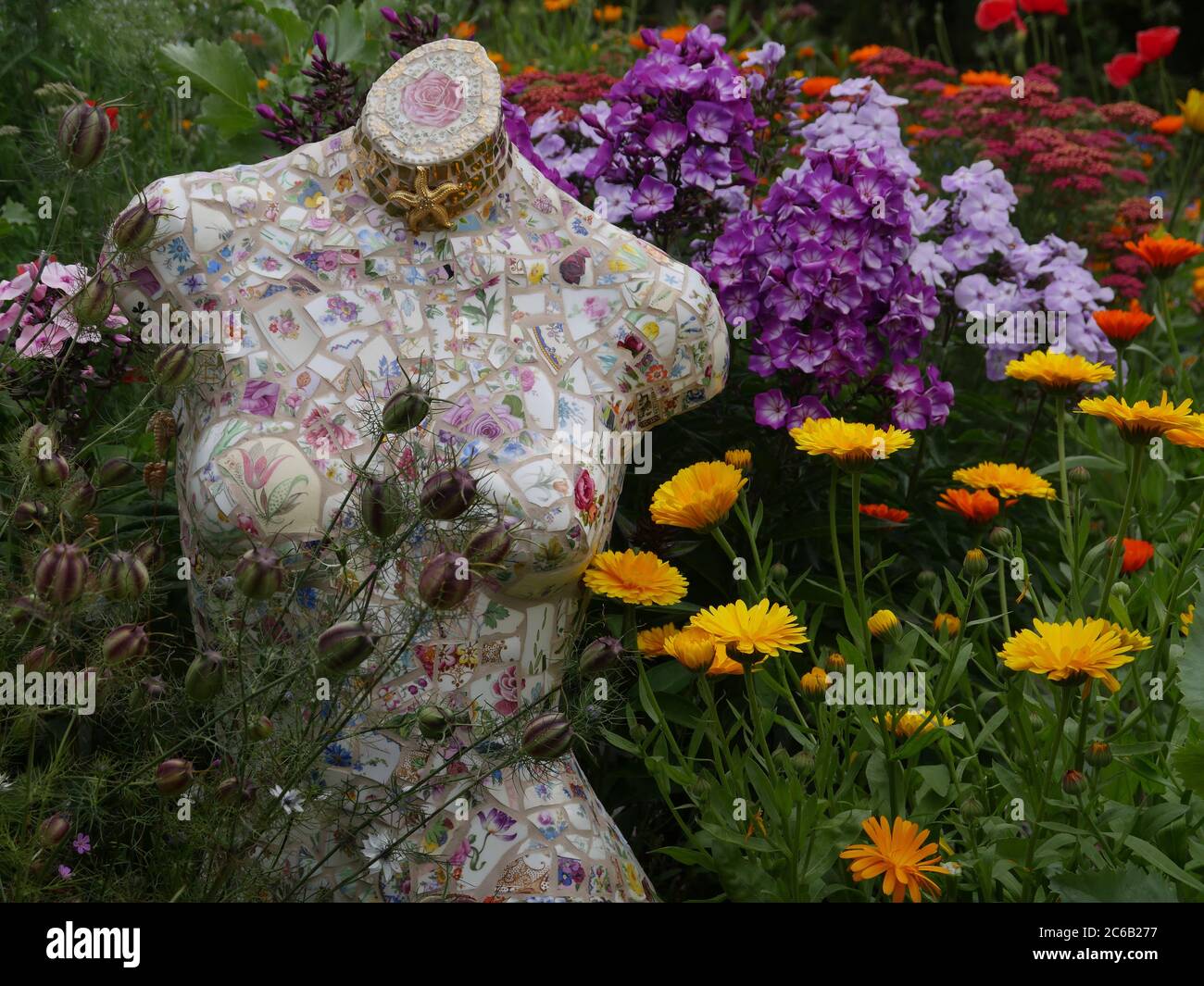 Mosaic garden sculpture of female torso surrounded by garden flowers ...
