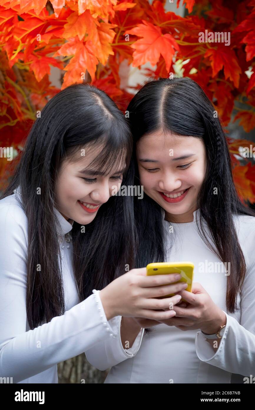 Two Vietnamese friends wearing traditional Ao Dai dresses and sharing a ...