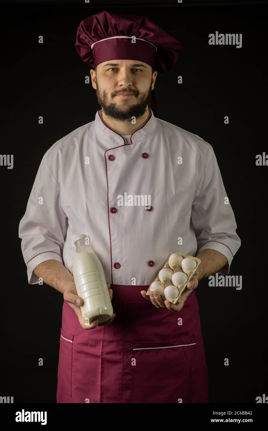 bearded Master chef in uniform holding bottle of milk and half dozen ...