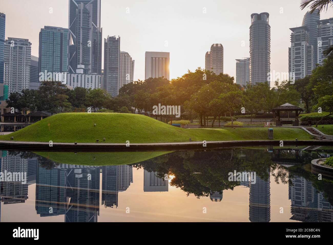 Kuala Lumpur skyline reflected in a still pond in KLCC Park at sunrise ...