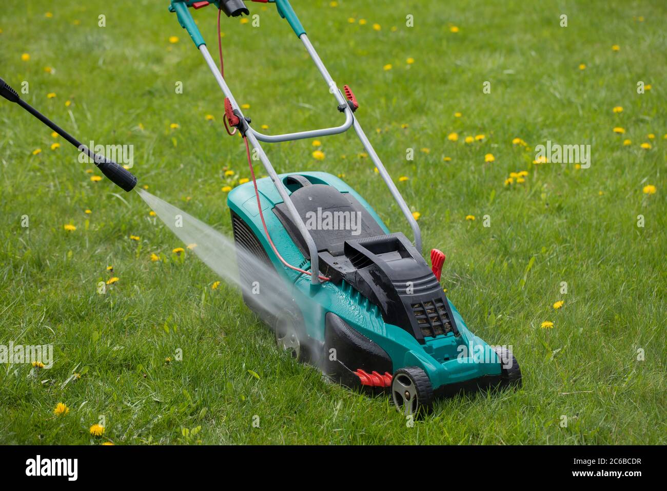 high-pressure washer washes lawn mower with jet of water on green grass ...
