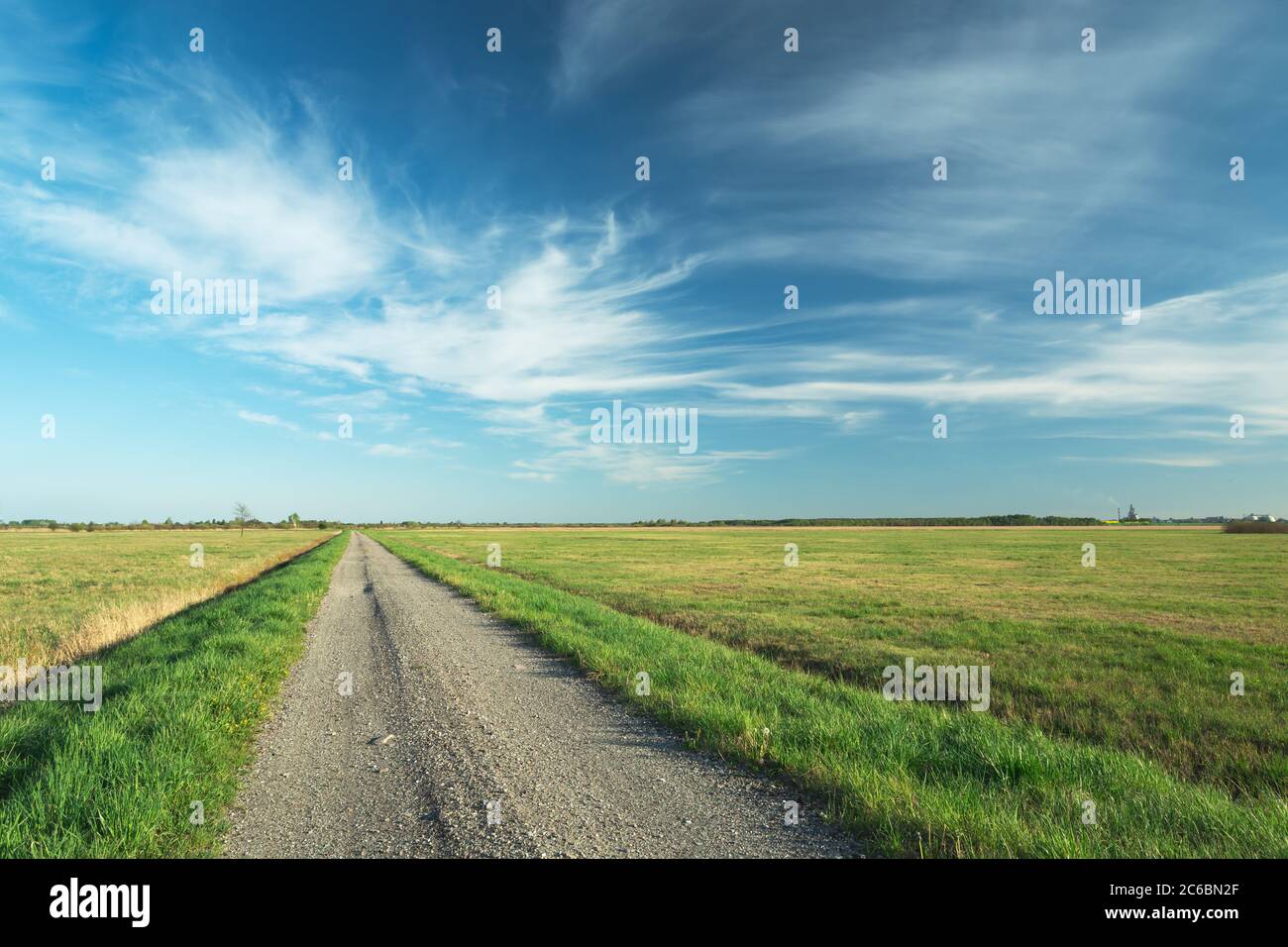 Gravel road on flat terrain and white clouds on blue sky, view in sunny ...